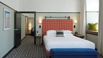 Quarto de hotel com uma cama grande, cabeceira, mesas de cabeceira, janela com cortinas e piso com padrão de tijolos.