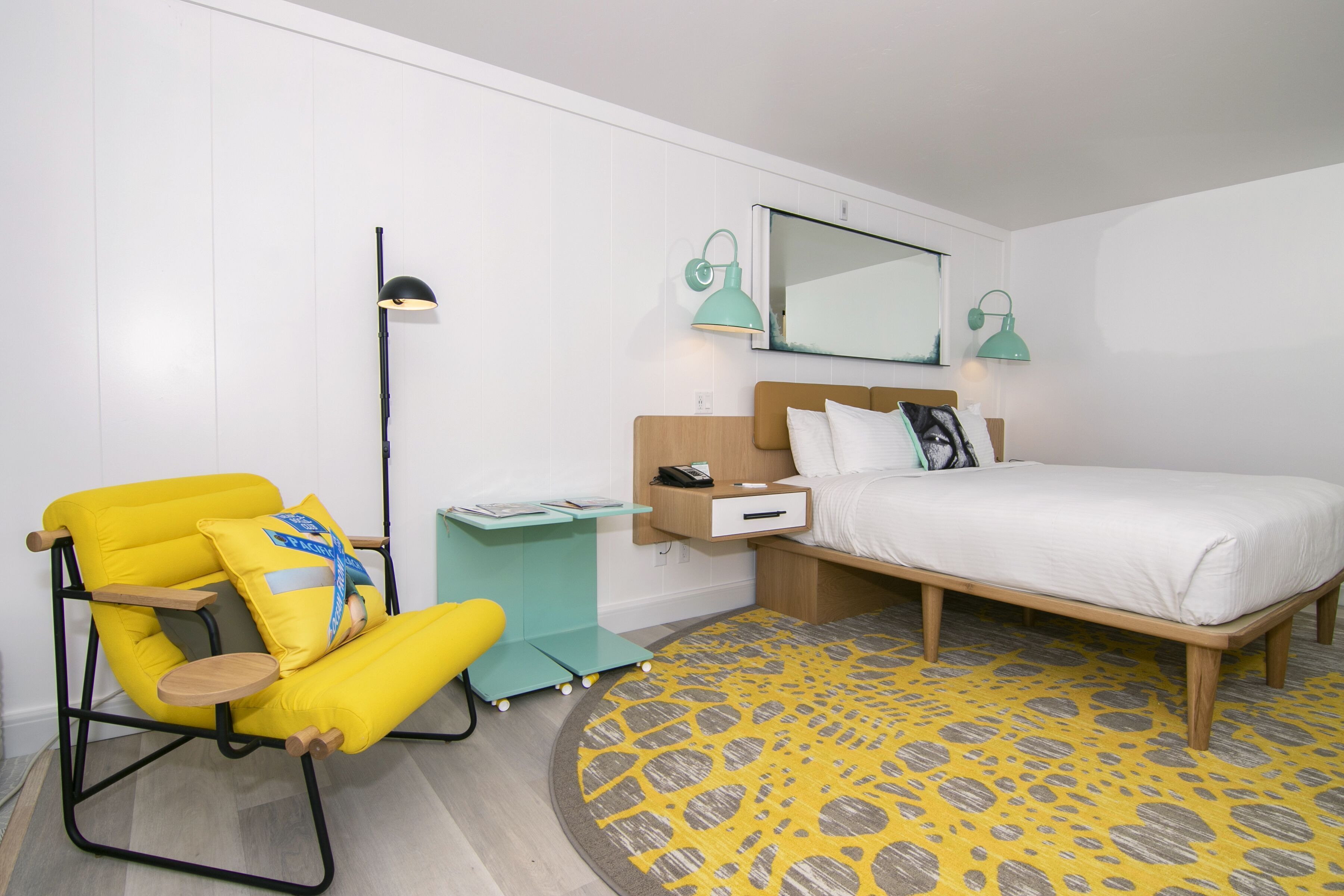 Quarto de hotel com uma cama, poltrona amarela, escrivaninha e espelho.