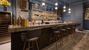 Uma área de bar com bancada de mármore, vários bancos altos e uma variedade de garrafas e copos.
