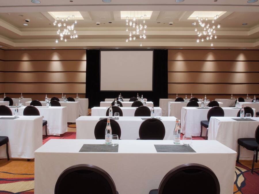 Uma sala de conferências com várias mesas, cadeiras e uma tela grande na frente.