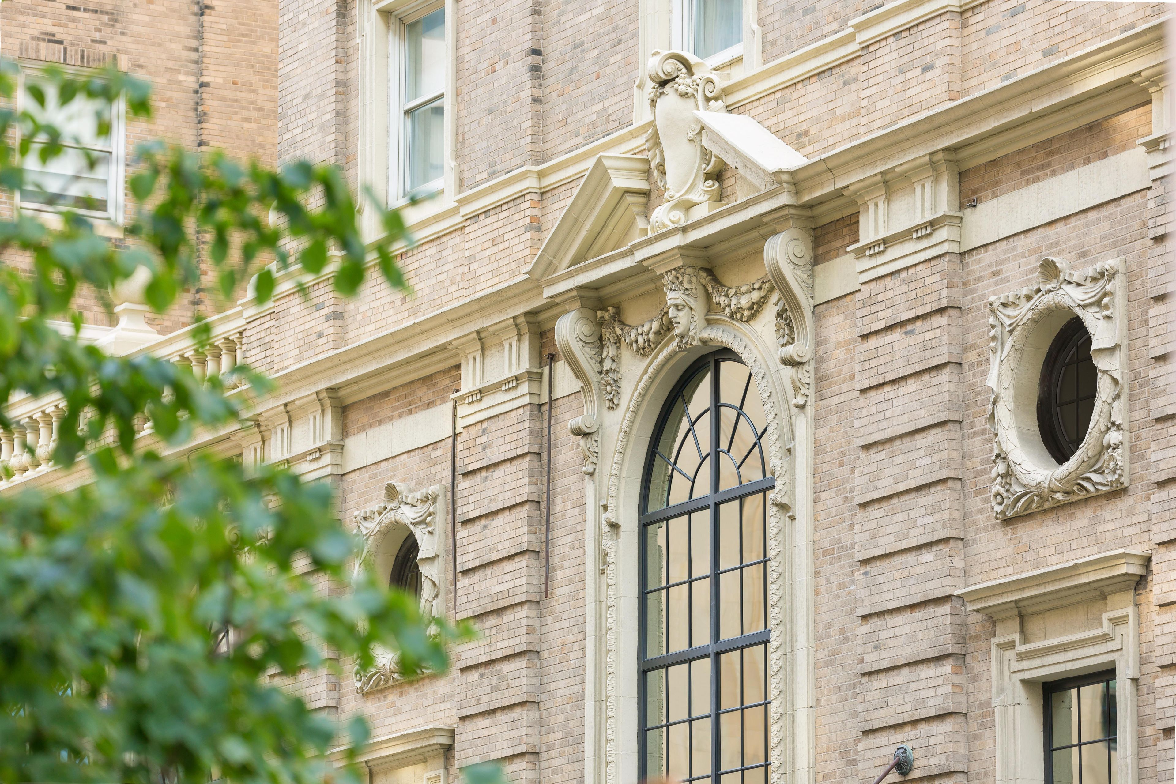 Fachada de edifício com detalhes arquitetônicos ornamentados, incluindo uma grande janela em arco e trabalho em pedra decorativo.