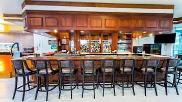 Uma área de bar com balcão alto, vários bancos e uma variedade de garrafas e copos.