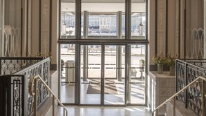 Uma entrada imponente com um grande candelabro, uma porta de vidro que dá para o exterior e piso de mármore.