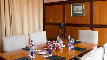 Uma sala de conferências com uma mesa de madeira, quatro cadeiras estofadas, um candelabro, um telefone e um quadro na parede.