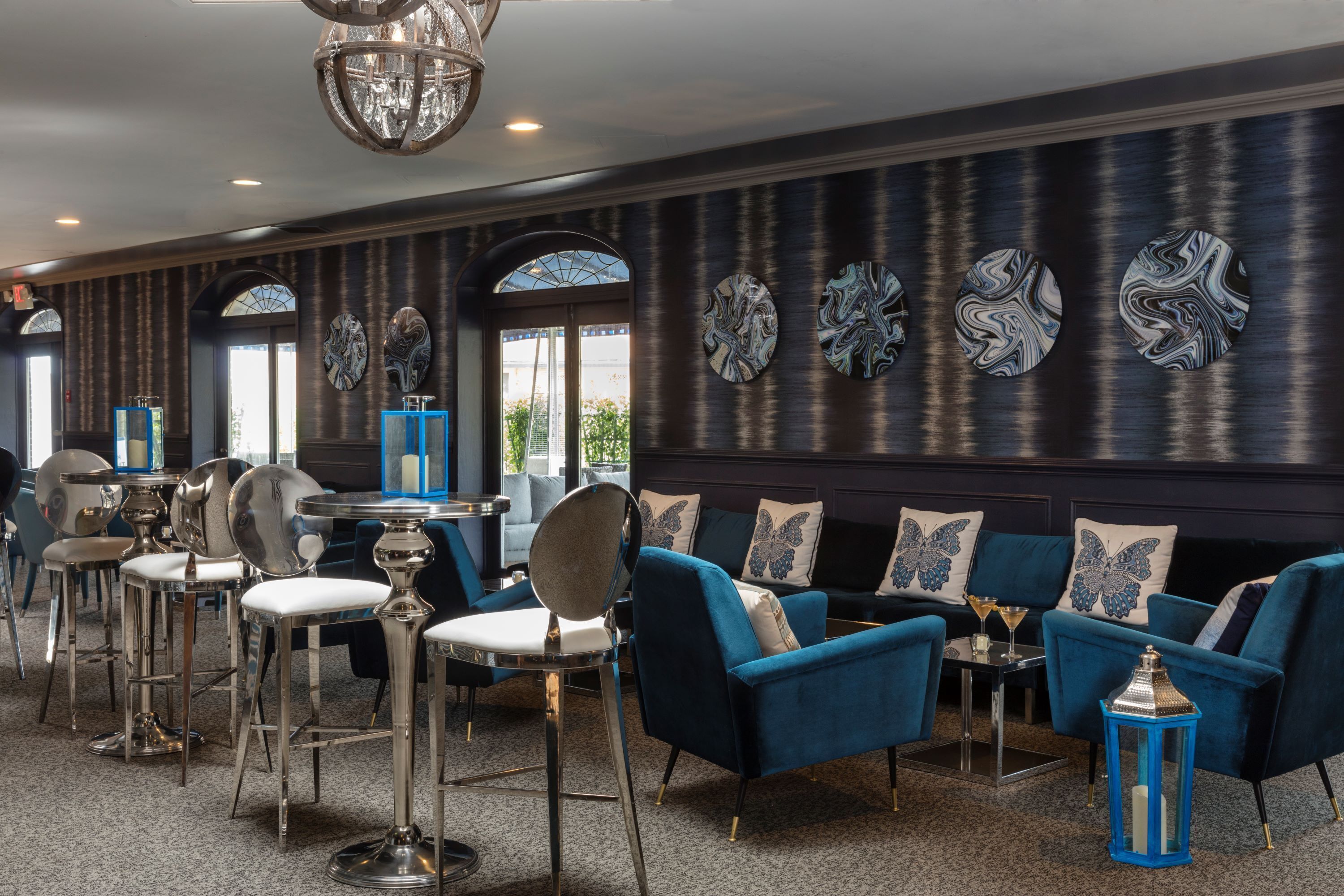 Uma área de estar moderna com sofás estofados azuis, um espaço de bar com banquetas altas e arte decorativa na parede.