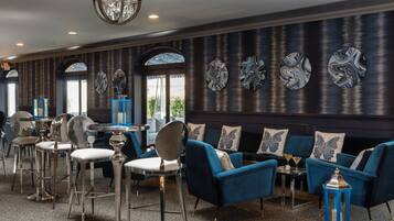 Uma área de estar moderna com sofás estofados azuis, um espaço de bar com banquetas altas e arte decorativa na parede.