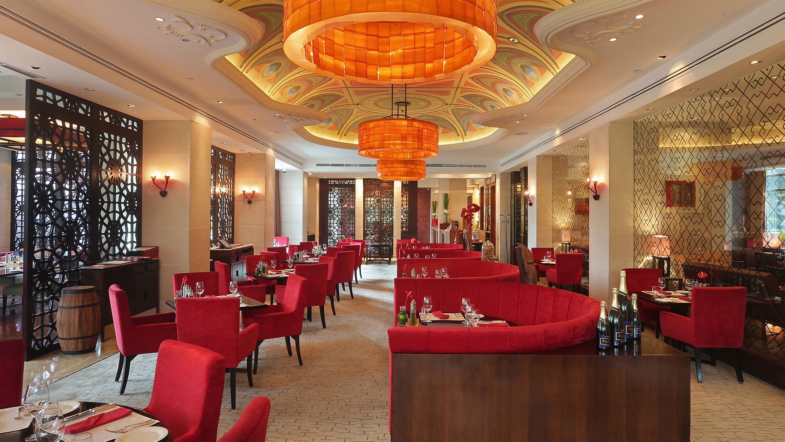 Um restaurante espaçoso com assentos em camarote estofados em vermelho e um lustre laranja no centro.