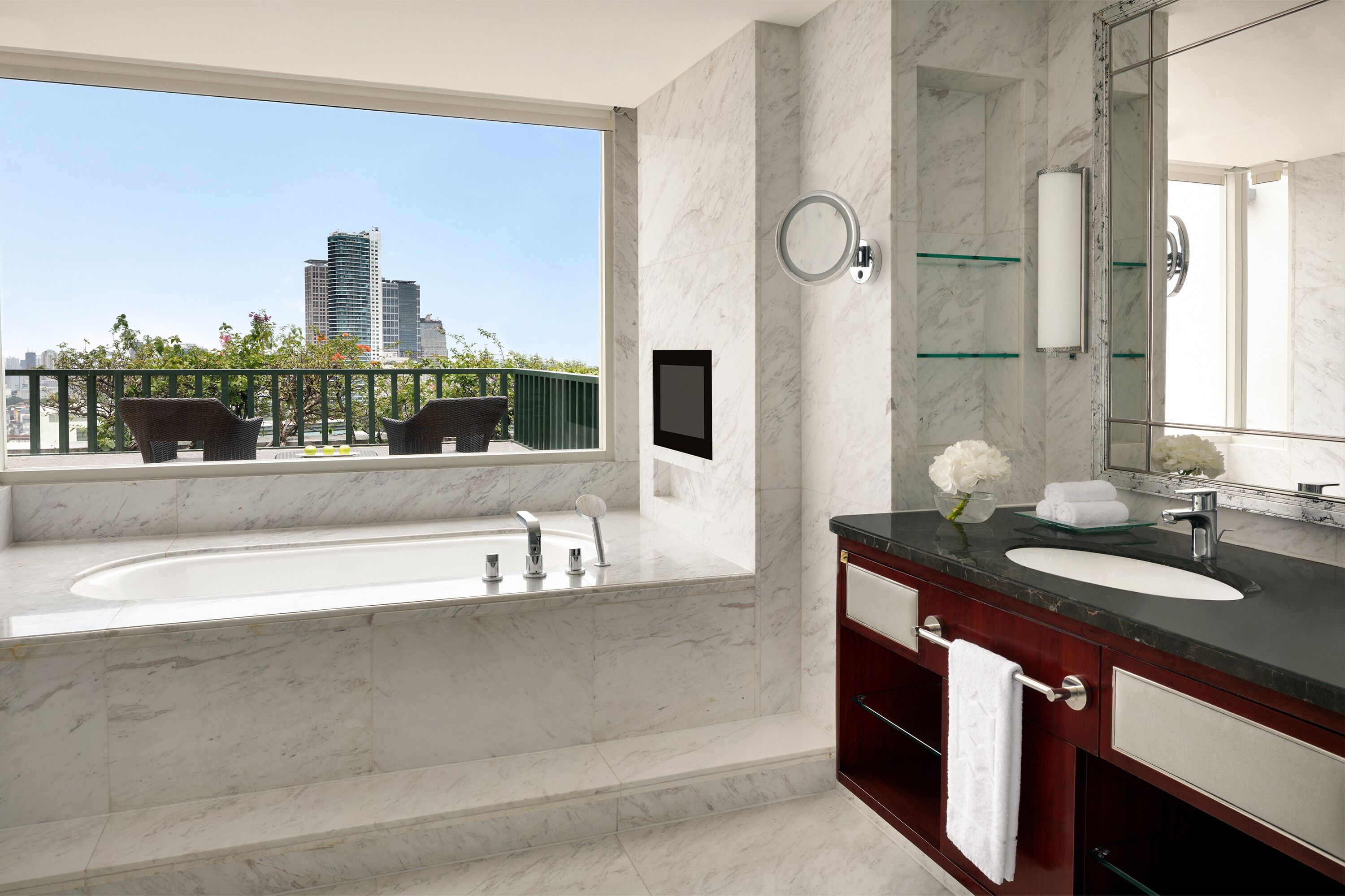 Uma casa de banho moderna com uma banheira grande, toucador com lavatório e um espelho amplo. Vê-se uma vista urbana pela janela.