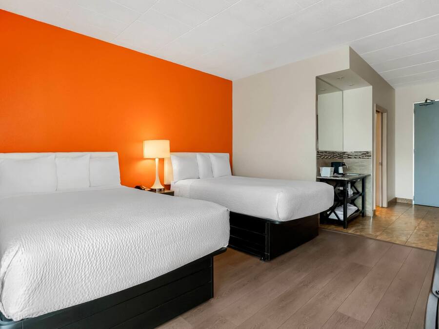 Quarto de hotel com duas camas, uma mesa de cabeceira com abajur, uma pequena mesa com pia e um espelho.