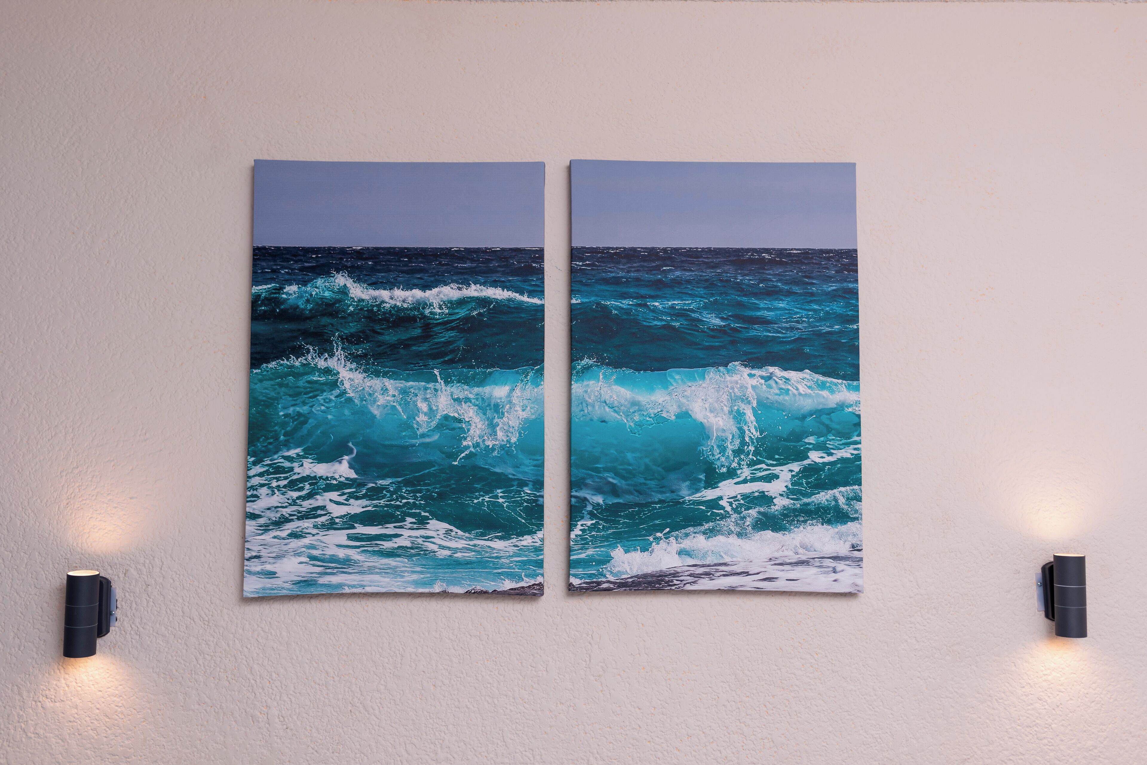 Paredes com duas grandes pinturas de uma paisagem oceânica azul, ladeadas por luminárias fixadas.