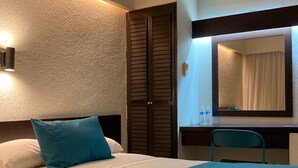 Quarto de hotel com cama, escrivaninha, cadeira, espelho e porta.