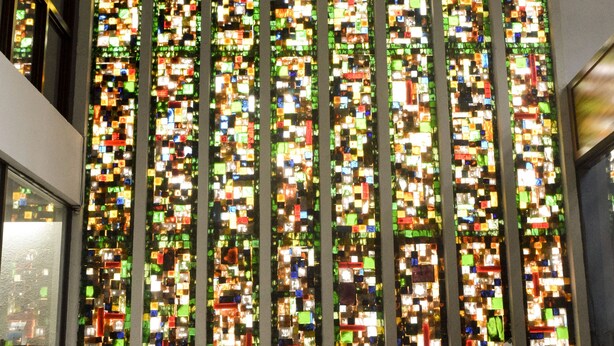 Interior moderno com um conjunto de sofás e uma mesa de centro em frente a uma parede de janelas coloridas, semelhantes a mosaicos.