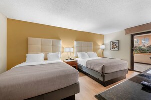 Quarto de hotel com duas camas, uma mesa pequena e vista para o exterior.