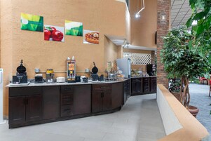 Uma cozinha com bancada, armários e diversos eletrodomésticos. Há decorações nas paredes, um vaso de planta e uma parede de tijolos.