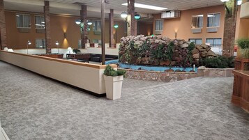 Um hall de hotel com balcão de recepção, parede de pedra com plantas e piso carpeteado.
