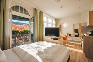 Quarto de hotel com cama, televisão, escrivaninha e varanda com vista para flores.