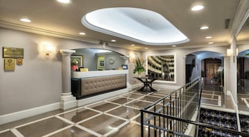 Um hall de hotel com recepção, relógio, espelho decorativo e escada.