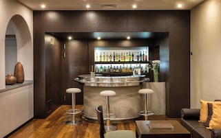 Uma área de bar com balcão circular, banquetas e diversos tipos de garrafas.