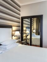 Quarto de hotel com cama, abajures, um espelho e parede listrada.