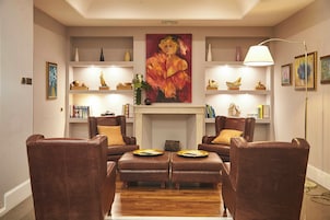 Uma sala de estar com lareira, poltronas de couro, uma mesa de centro e um quadro sobre a lareira.
