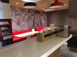 Um restaurante moderno com uma área de assentos em camarote vermelho, um balcão branco com um laptop e luminárias pendentes.
