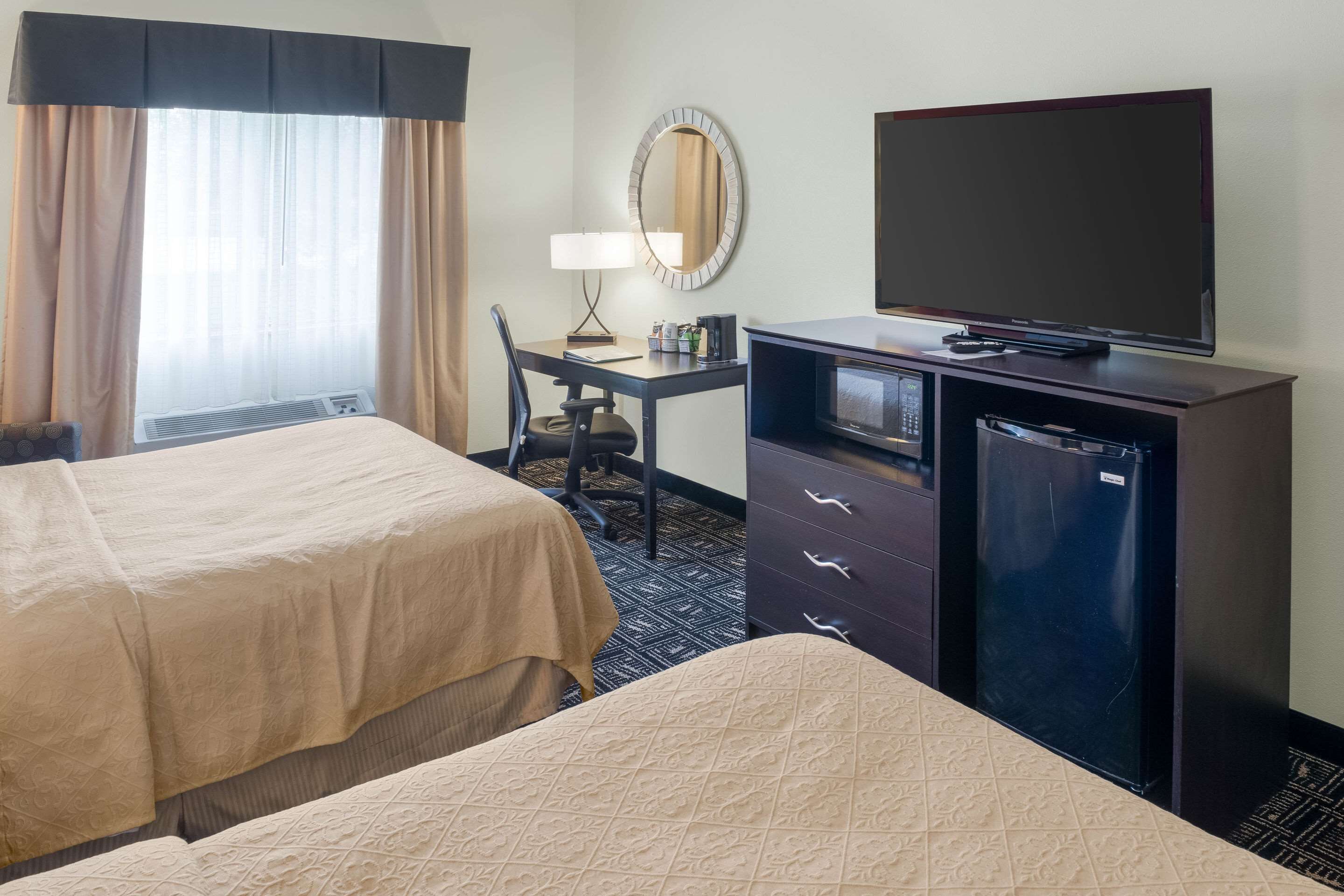 Quarto de hotel com duas camas, uma escrivaninha com cadeira, televisão, espelho e um frigorífico.