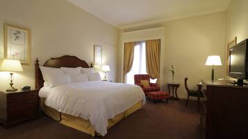 Quarto de hotel com uma cama grande, mesas de cabeceira com abajures, uma escrivaninha com televisão e uma cadeira.