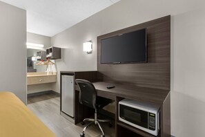 Quarto de hotel compacto com cozinha compacta, TV de tela plana na parede, escrivaninha com cadeira e micro-ondas.