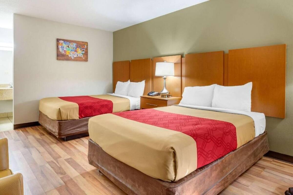 Quarto de hotel com duas camas, uma mesa de cabeceira com abajur, cabeceira de madeira e um mapa na parede.