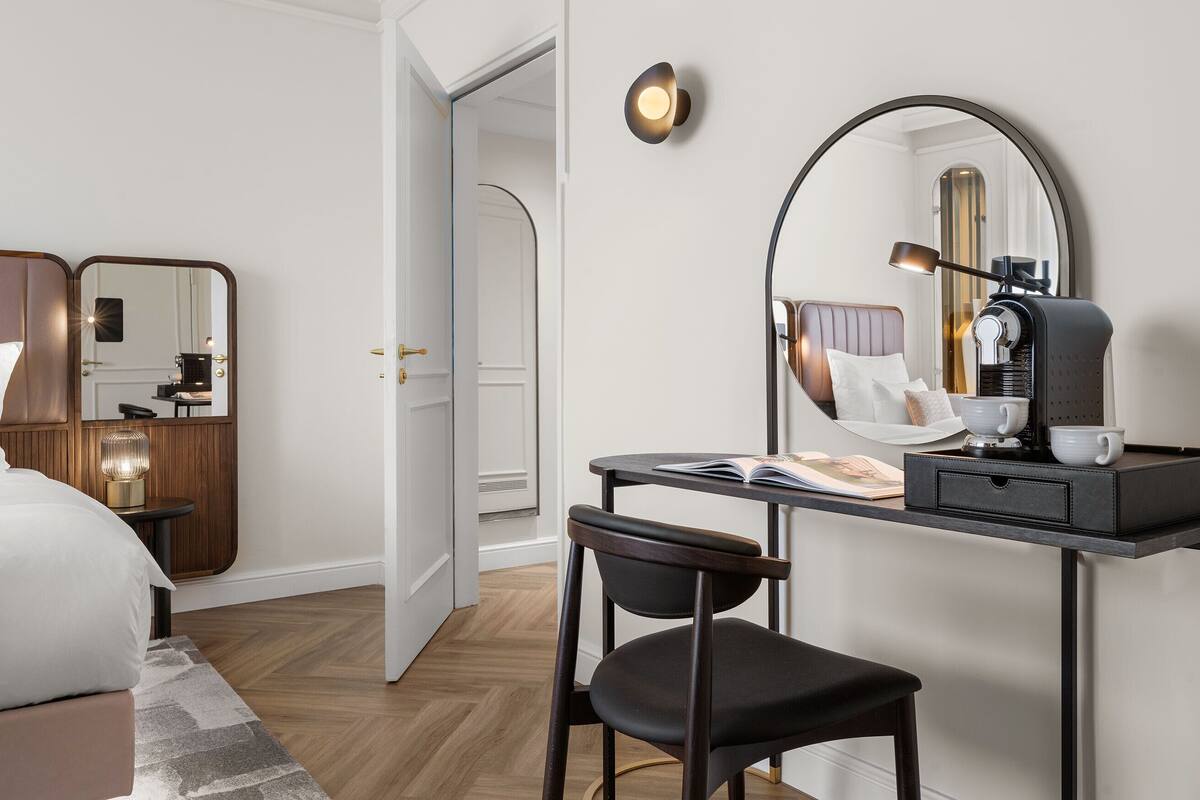 Quarto de hotel com uma cama, uma escrivaninha com cadeira, um espelho e uma máquina de café.