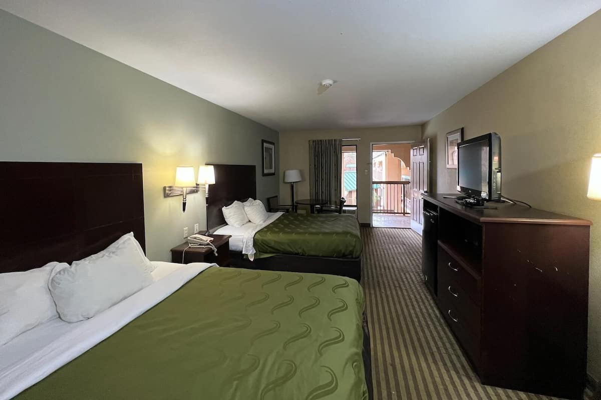Quarto de hotel com duas camas, uma mesa de trabalho com televisão e vista para o exterior.