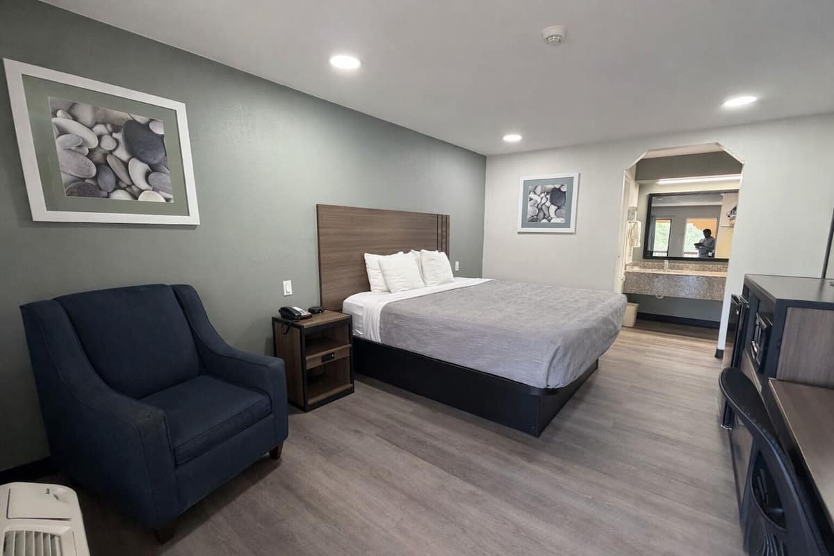 Quarto de hotel com cama, poltrona, mesa de cabeceira e escrivaninha.