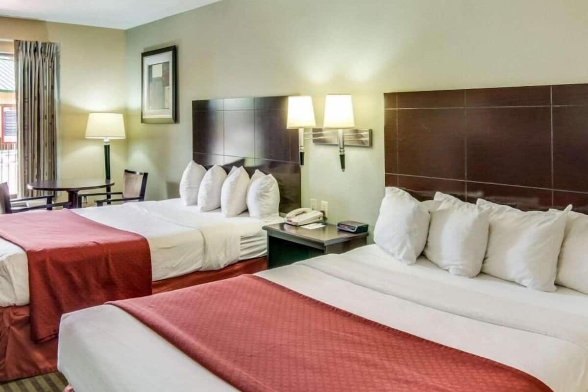 Quarto de hotel com duas camas, uma mesa, uma cadeira, uma televisão e uma janela com cortinas.