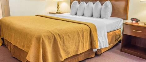 Quarto de hotel com uma cama grande, cabeceira de madeira, duas luminárias de cabeceira, mesa de apoio e um quadro na parede.