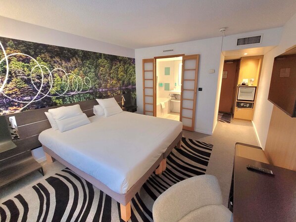 Quarto de hotel com cama, escrivaninha, cadeira, banheiro e televisão.