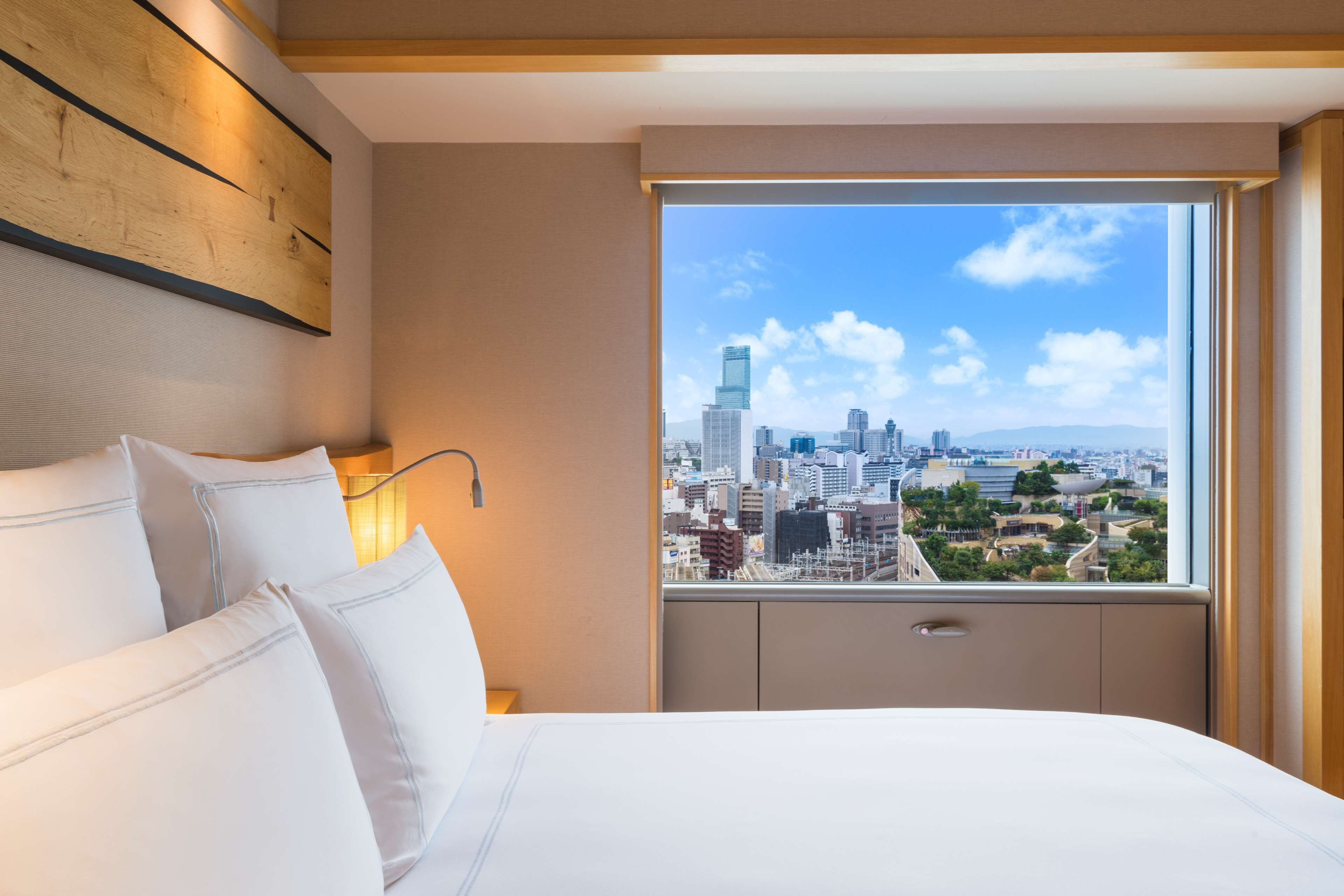 Quarto de hotel com uma grande janela e vista para a paisagem urbana.