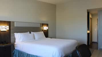 Quarto de hotel com uma cama grande, cabeceira de madeira, abajures e uma escrivaninha com cadeira.