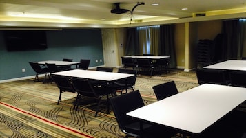 Sala de conferência com mesas, cadeiras, projetor e uma tela grande.