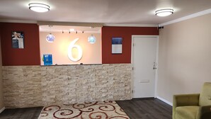 Uma área de recepção com parede de pedra, um número '6' iluminado e uma porta à direita.
