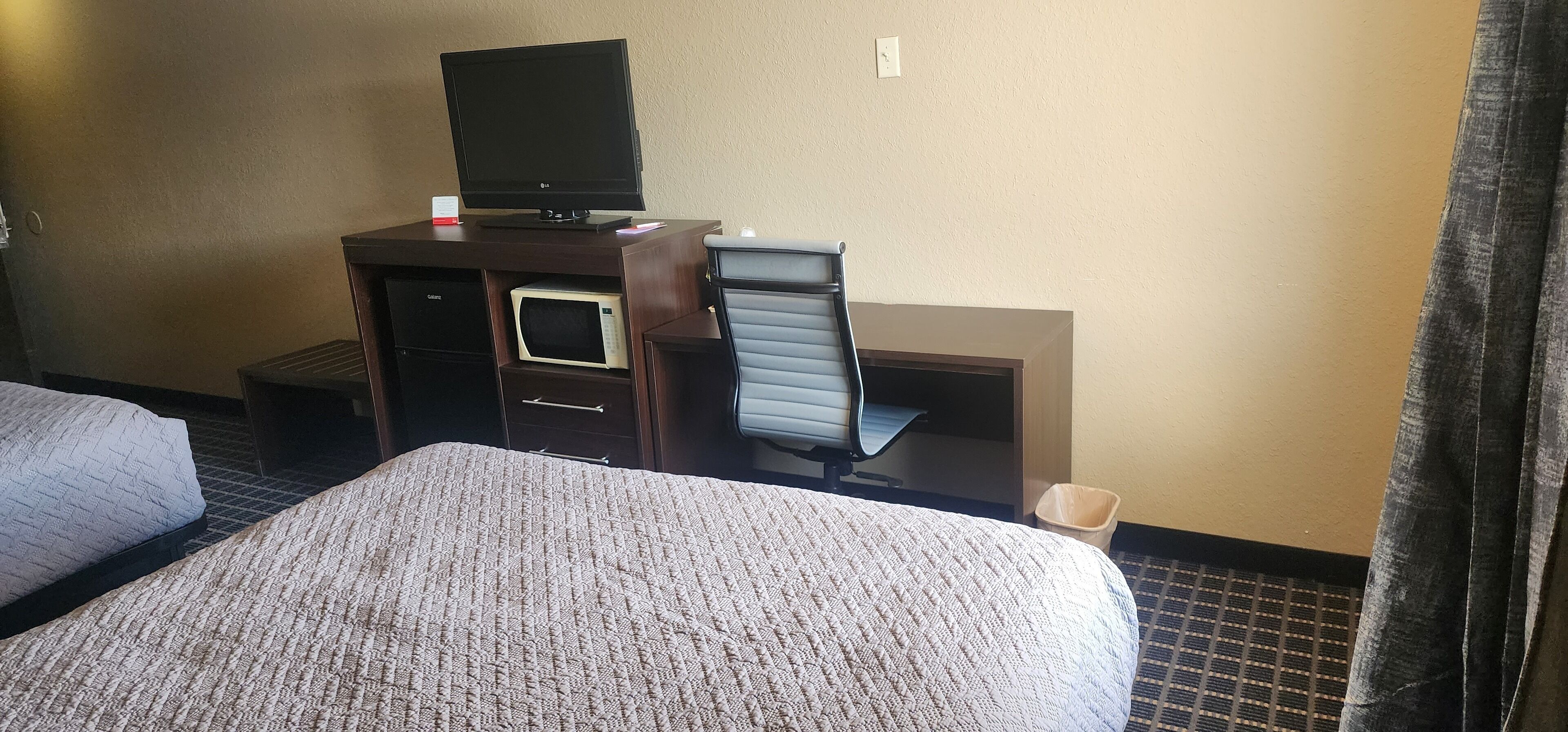 Quarto de hotel com duas camas, uma mesa de escritório com televisão, micro-ondas e lixeira.