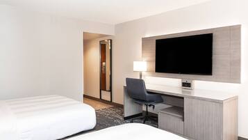 Quarto de hotel com duas camas, uma mesa com cadeira, uma televisão de tela plana e um abajur.