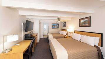 Quarto de hotel com cama, escrivaninha, cadeira, televisão e obra de arte na parede.