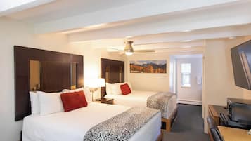 Quarto de hotel com duas camas, uma escrivaninha, televisão e ventoinha no teto.