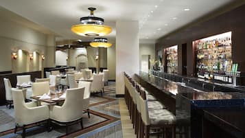 Uma área de bar de hotel com diversas opções de assento, um balcão extenso e uma variedade de bebidas.