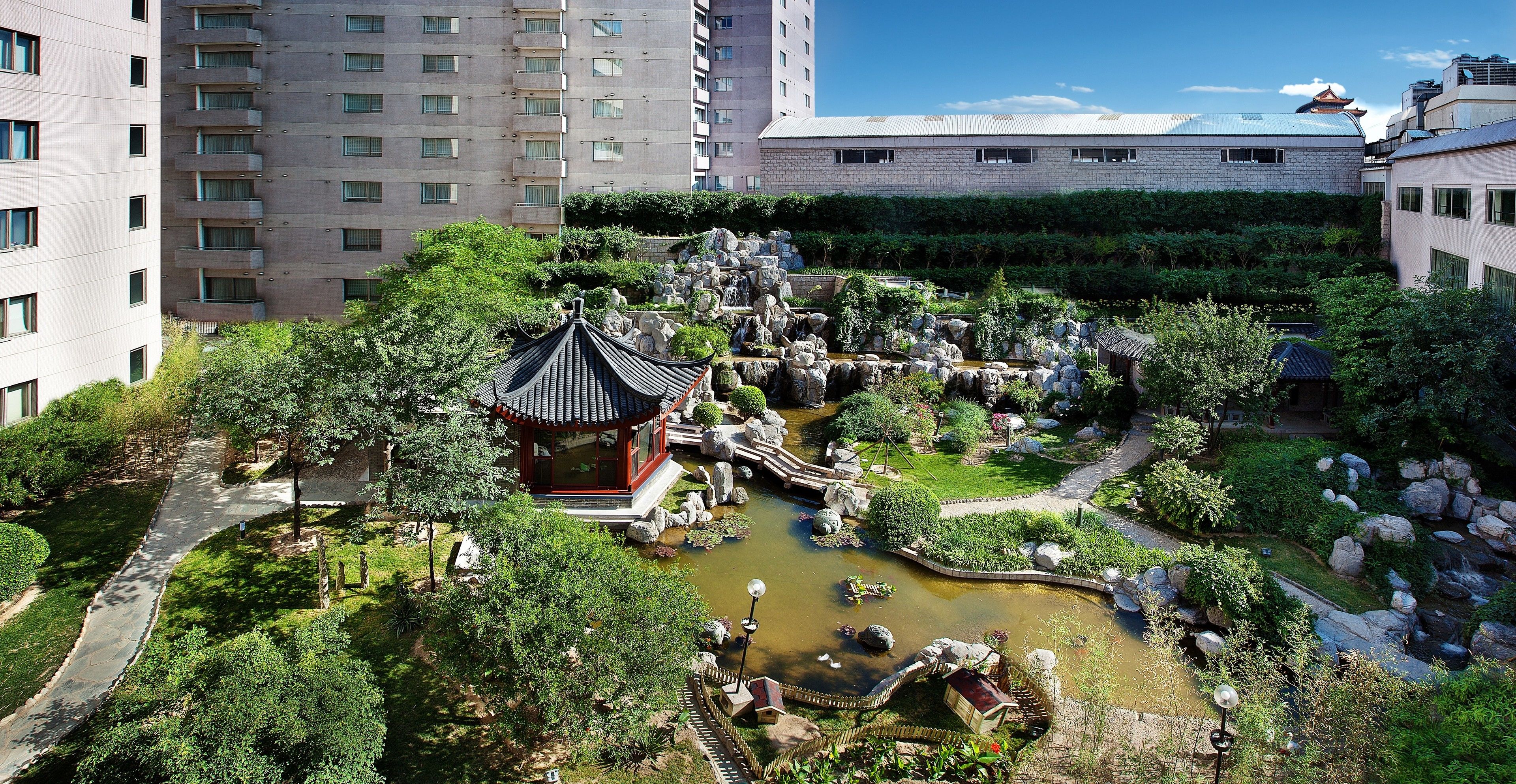 Um pavilhão de estilo tradicional rodeado por um jardim com lago, pedras e caminhos.