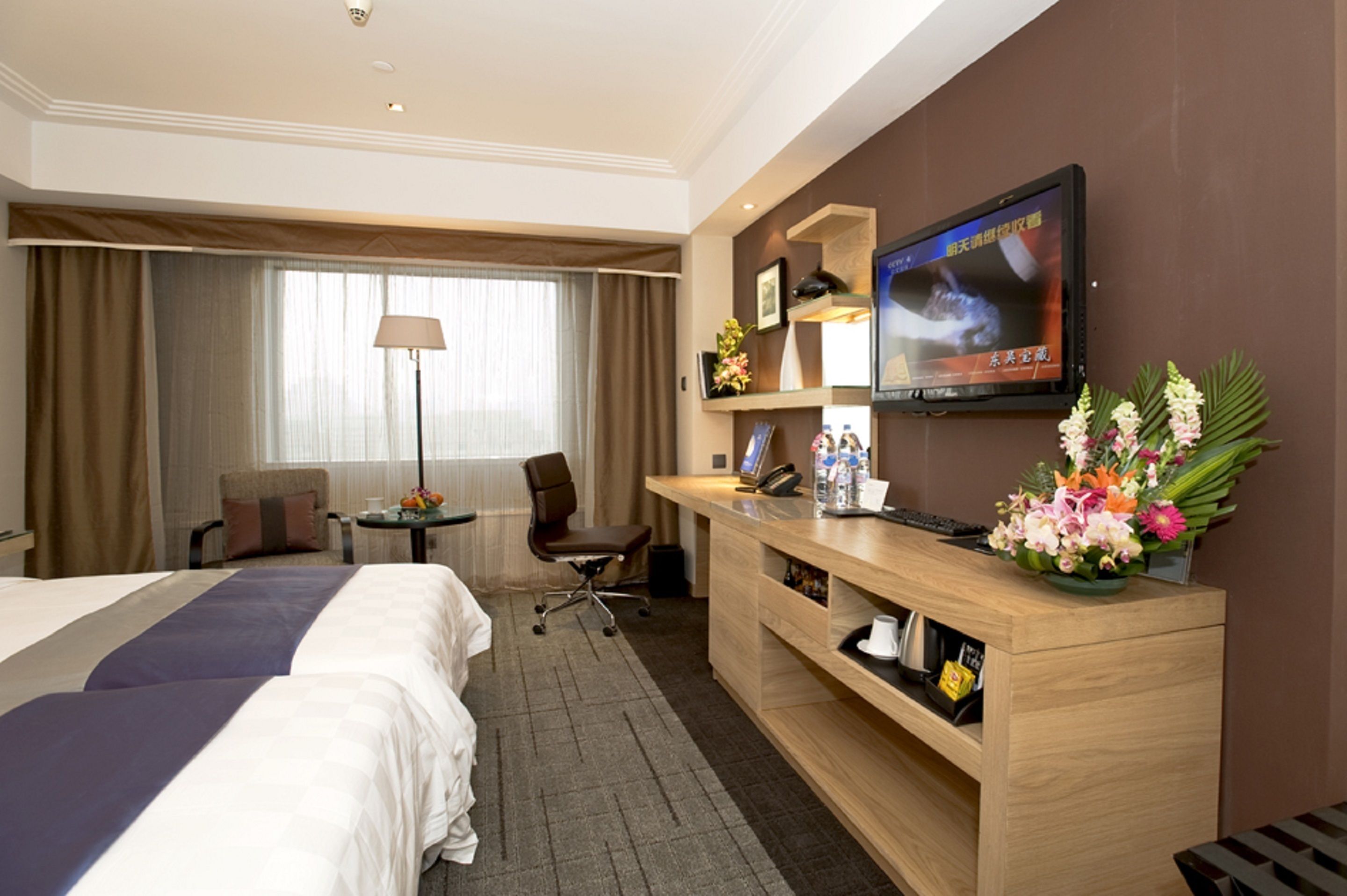 Quarto de hotel com uma cama grande, uma escrivaninha com computador, uma televisão na parede e uma luminária de mesa.