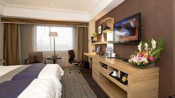 Quarto de hotel com uma cama grande, uma escrivaninha com computador, uma televisão na parede e uma luminária de mesa.