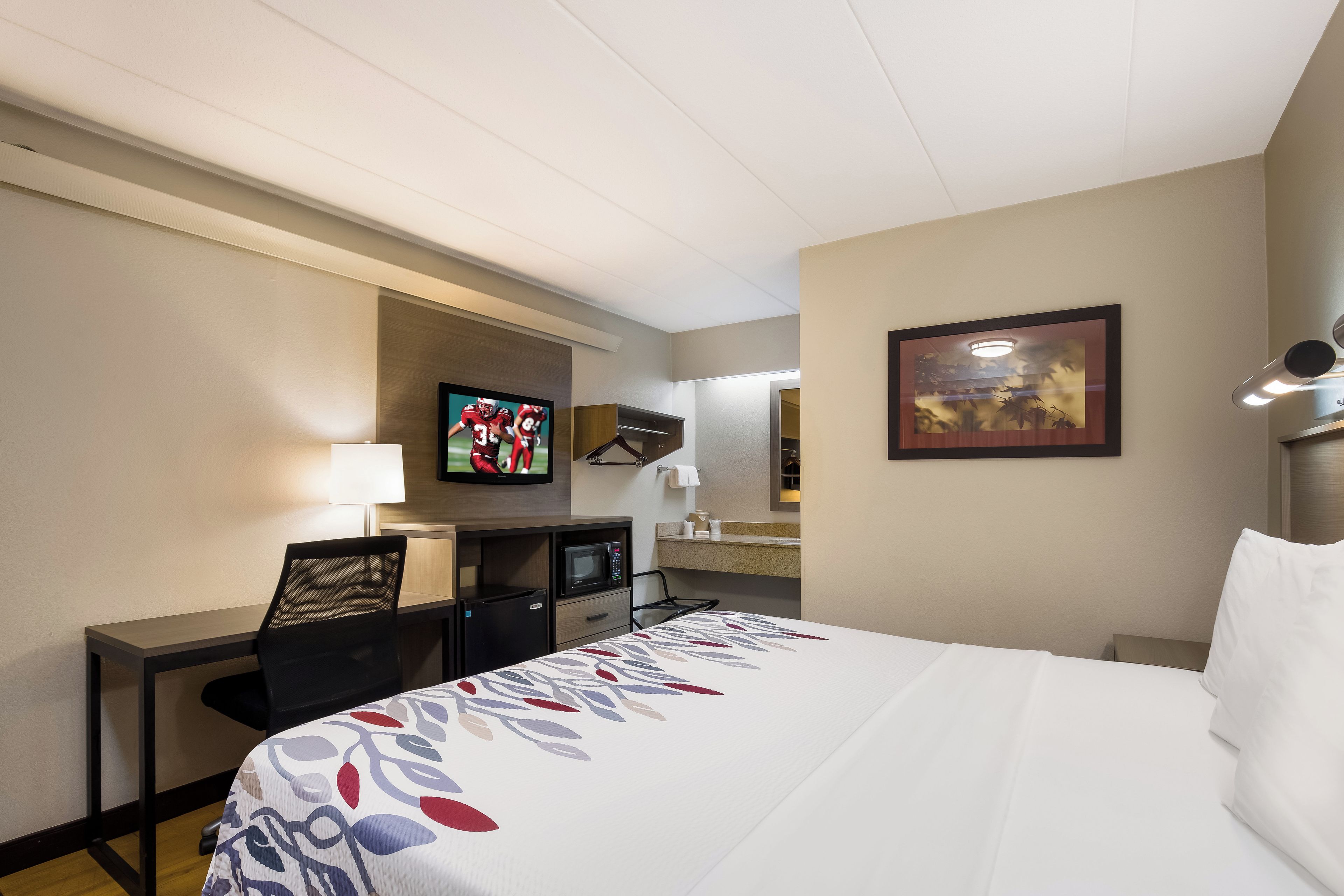 Quarto de hotel com cama, escrivaninha, cadeira, televisão e micro-ondas.