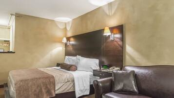Quarto de hotel com cama, mesa de cabeceira, sofá de couro e luminária fixada na parede.