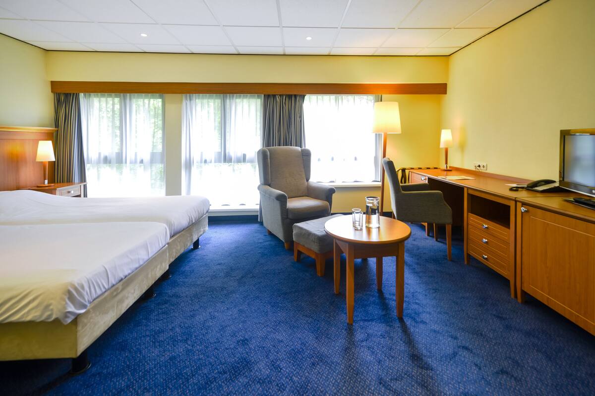 Quarto de hotel com duas camas, uma escrivaninha, uma cadeira, uma mesinha e uma televisão.